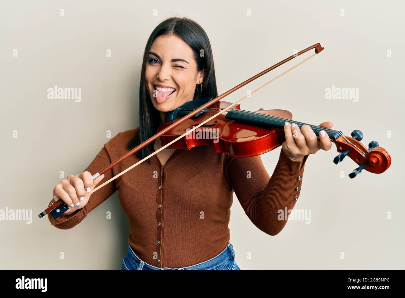 Young brunette woman playing violin sticking tongue out happy with ...