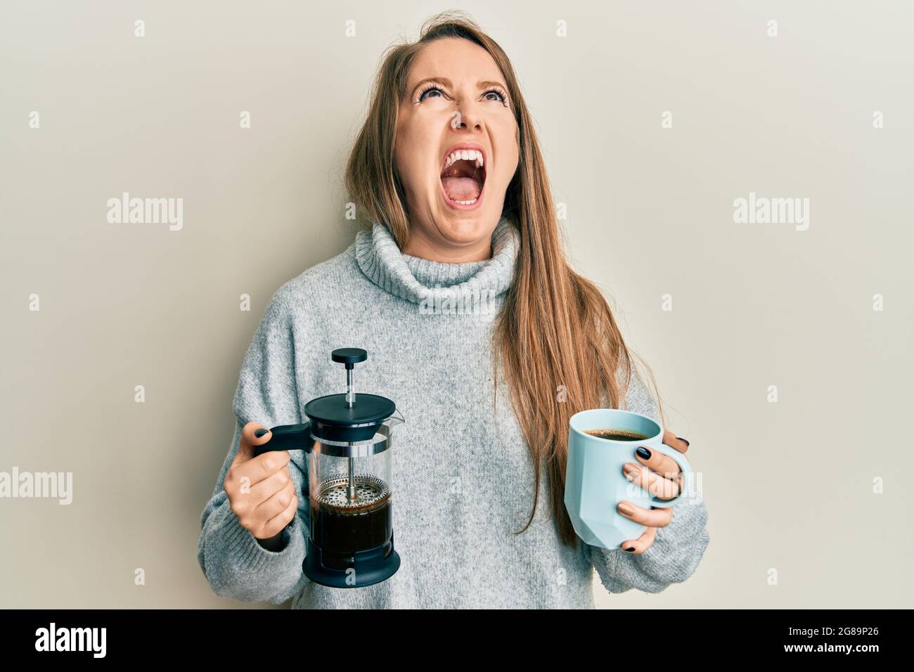Young blonde woman drinking a cup of italian coffee angry and mad ...