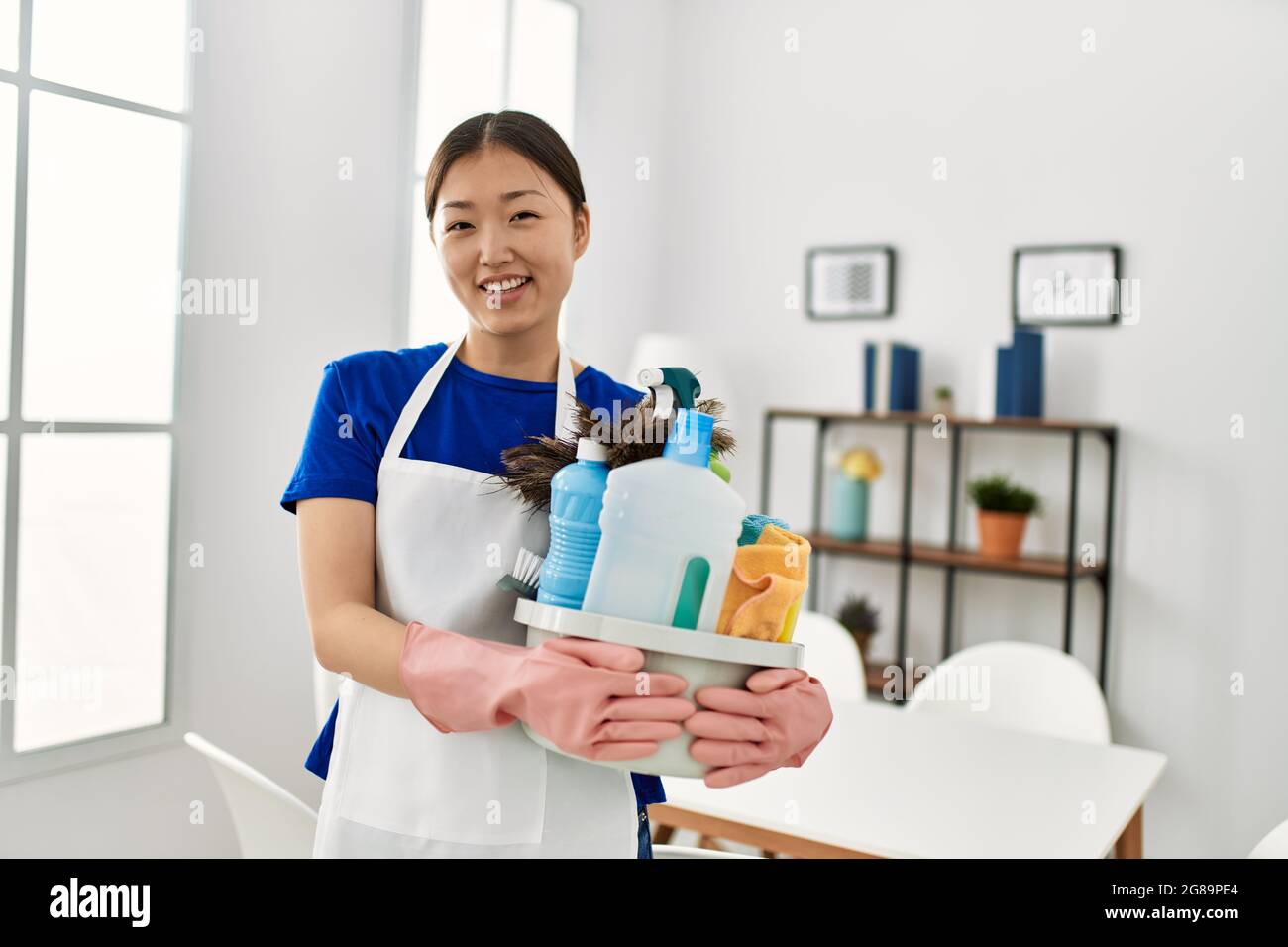 Young chinese housewife holding cleaning products standing at home ...