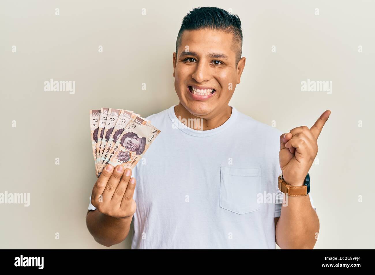 Young latin man holding 500 mexican pesos banknotes smiling happy ...
