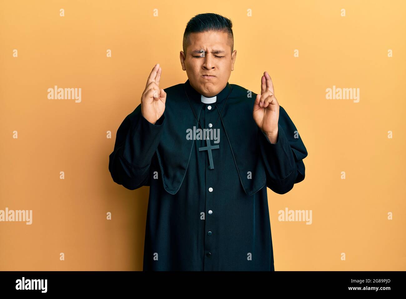 Young latin priest man standing over yellow background gesturing finger ...