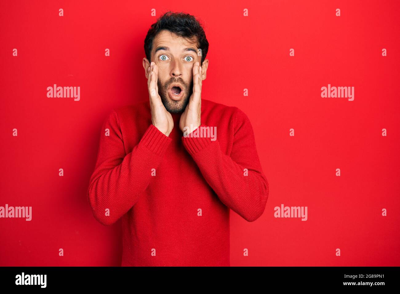 Handsome man with beard wearing casual red sweater afraid and shocked ...