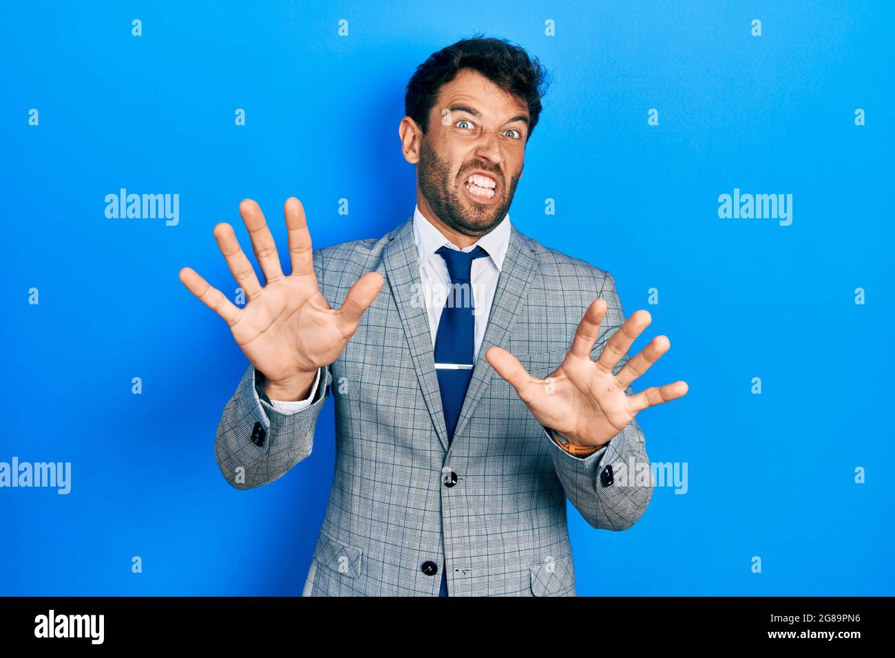 Handsome man with beard wearing business suit and tie afraid and ...