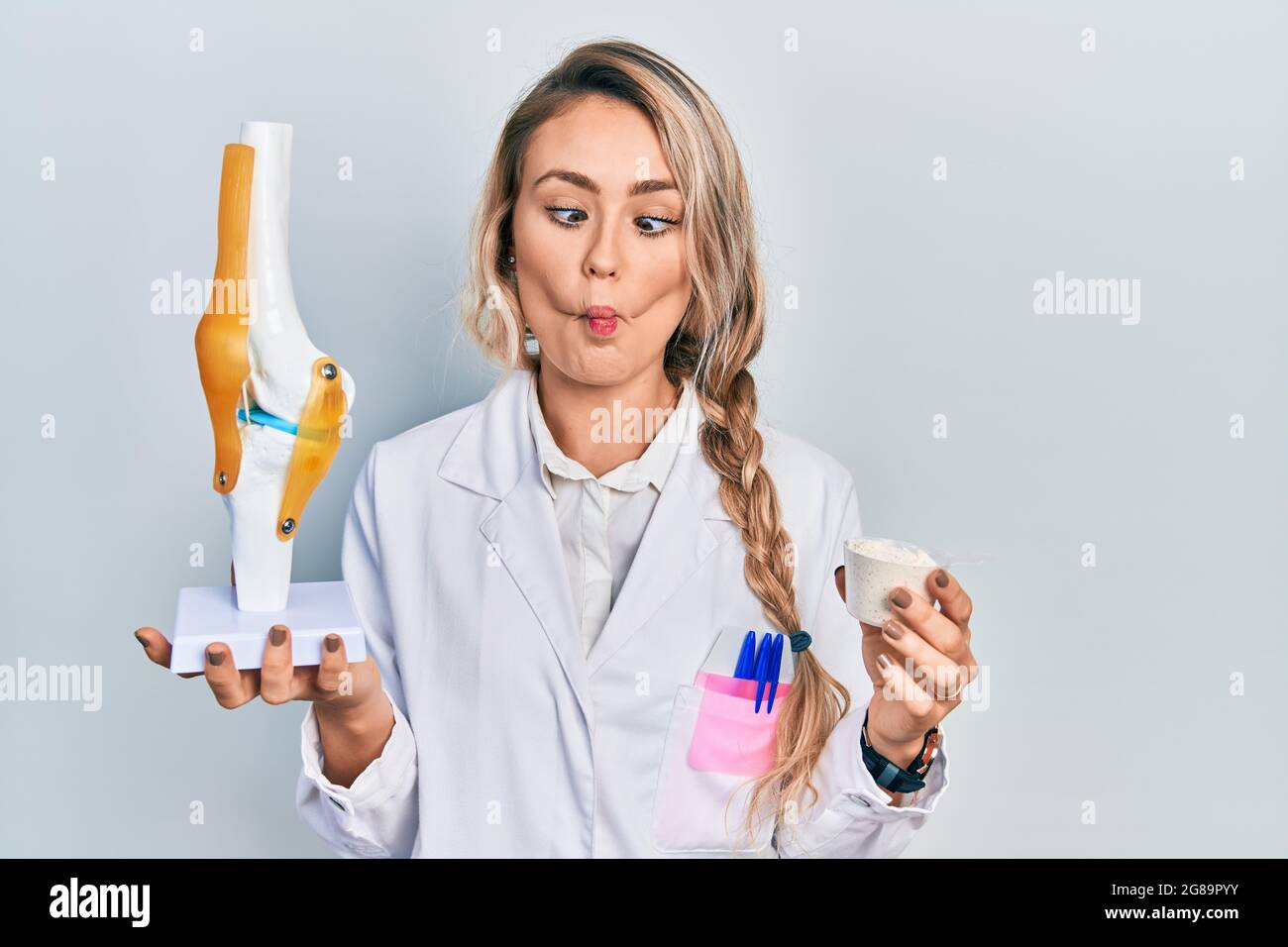 Beautiful young blonde doctor woman holding anatomical model of knee ...