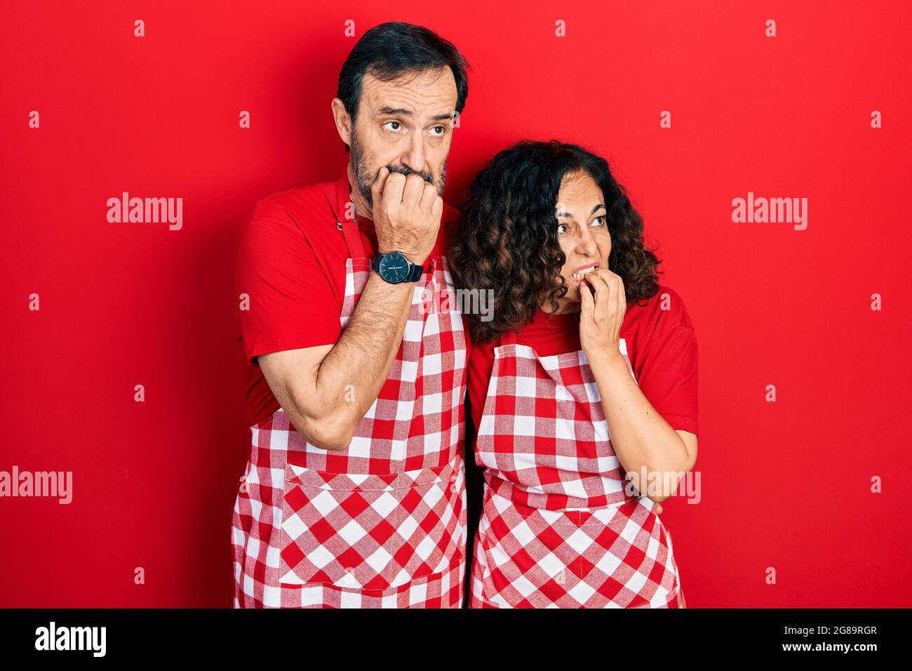 Middle age couple of hispanic woman and man wearing cook apron looking ...