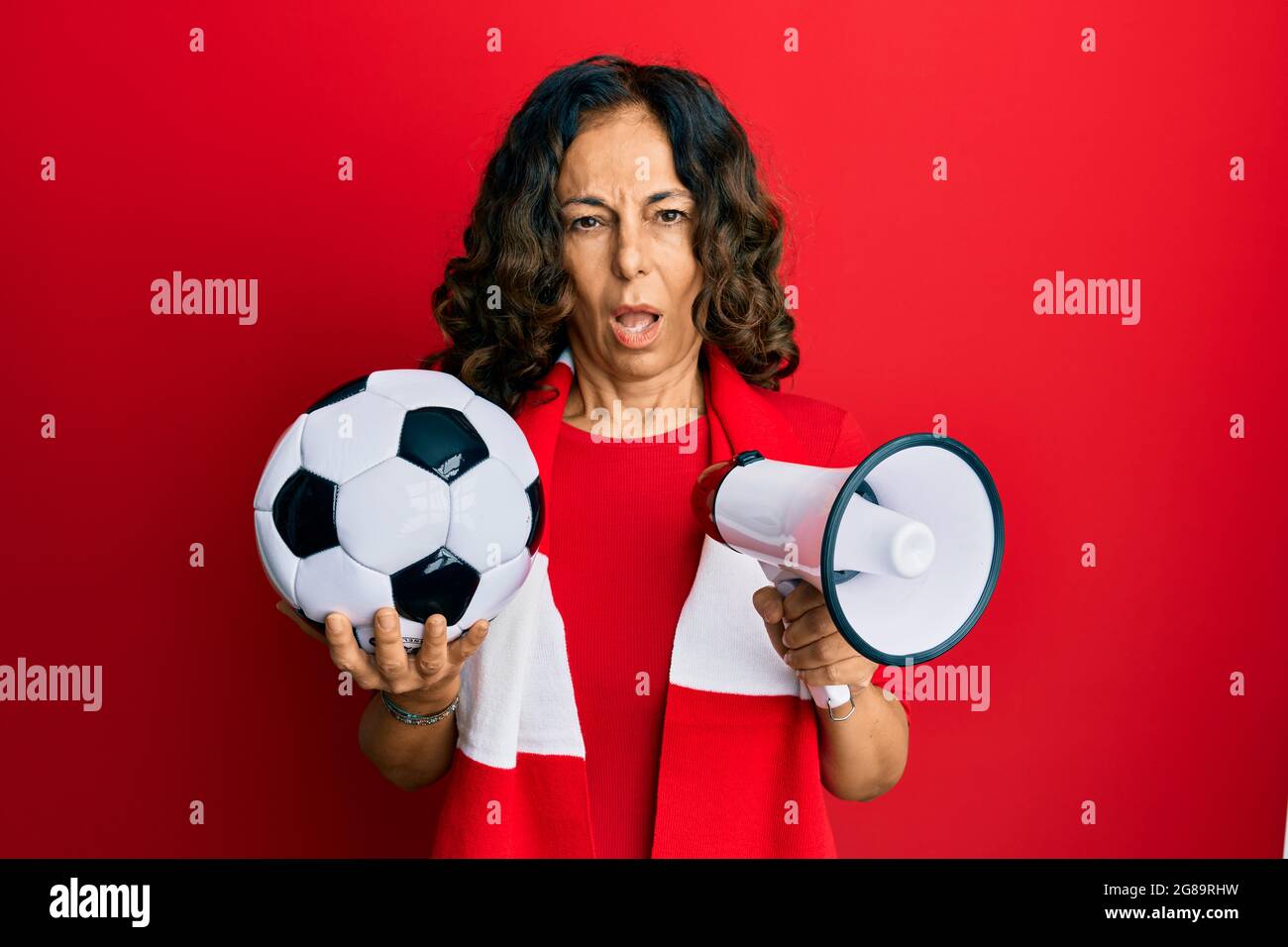 Middle age hispanic woman football hooligan holding ball and using ...