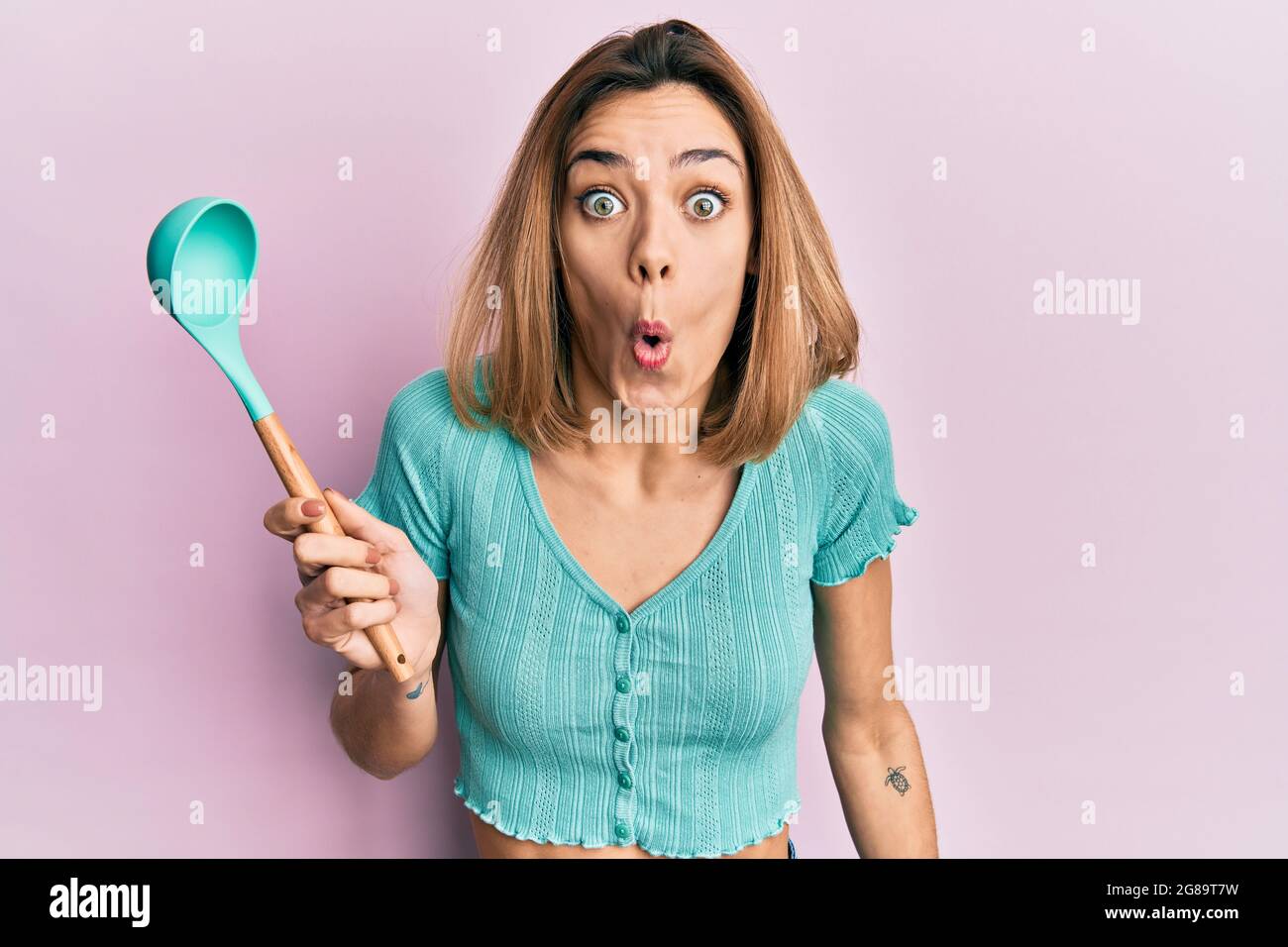 Young caucasian blonde woman holding silicone soup spoon scared and ...