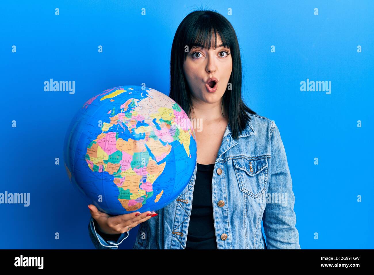 Young hispanic woman holding world ball scared and amazed with open ...