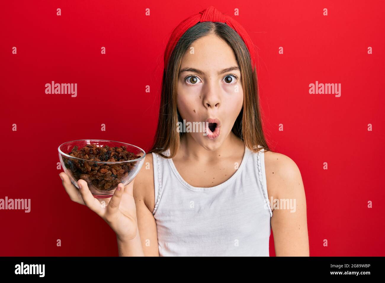Beautiful brunette little girl holding bowl of raisins scared and ...