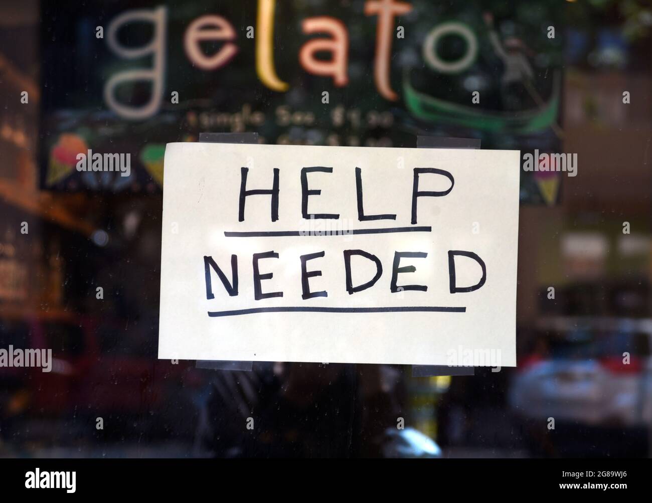 A Help Wanted sign taped to the windwo of a ice cream and gelato parlor ...