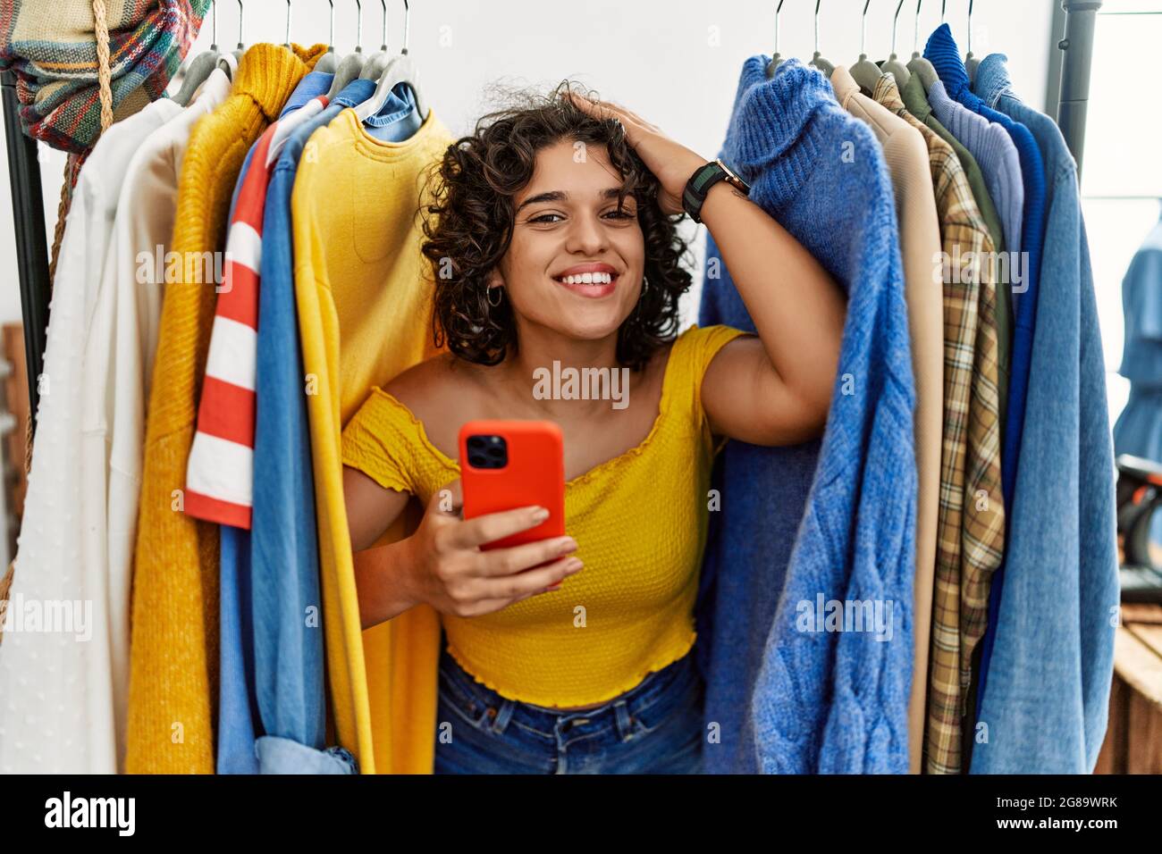 Young hispanic woman searching clothes on clothing rack using ...
