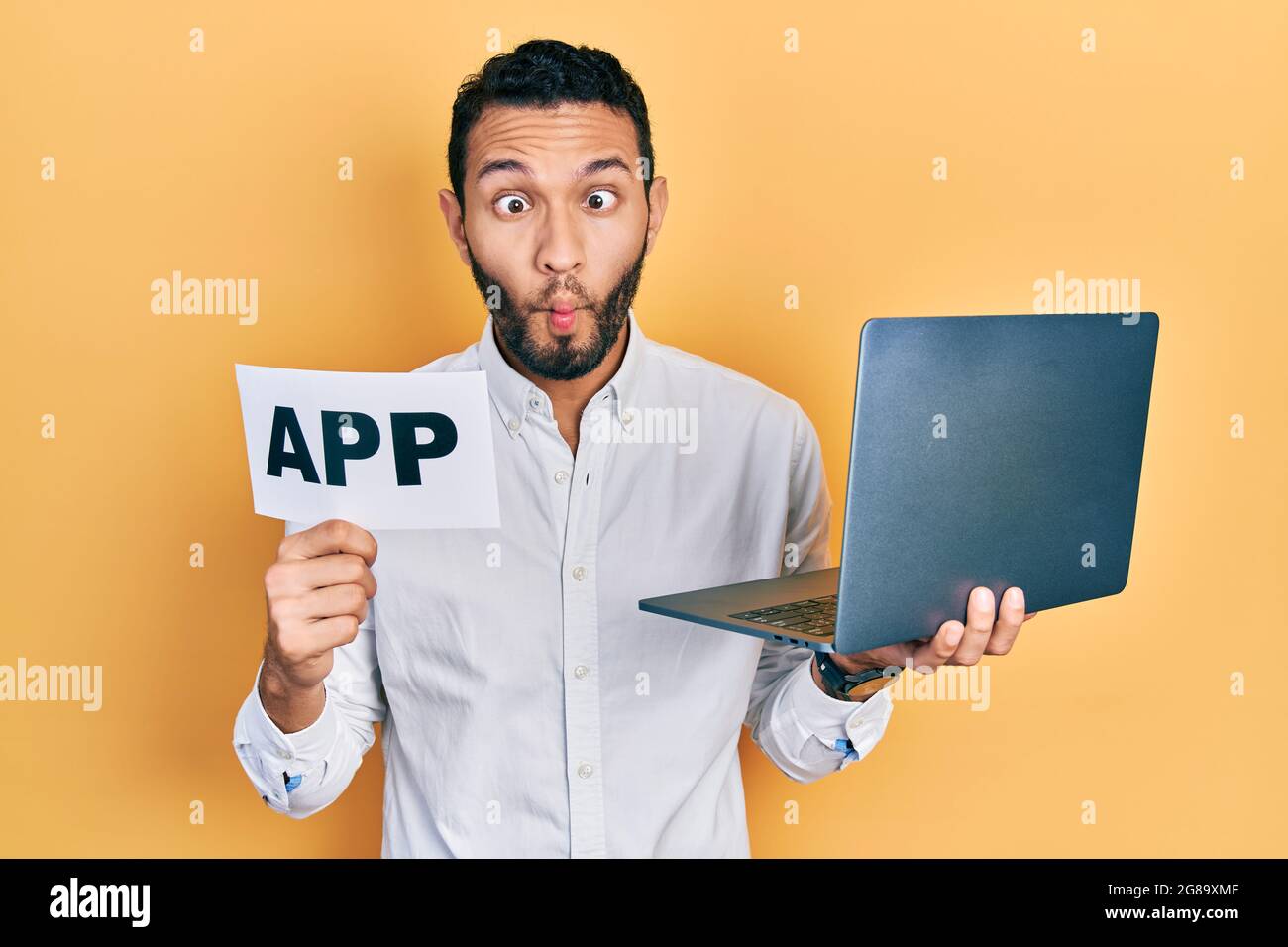 Hispanic man with beard holding computer laptop and app banner making ...