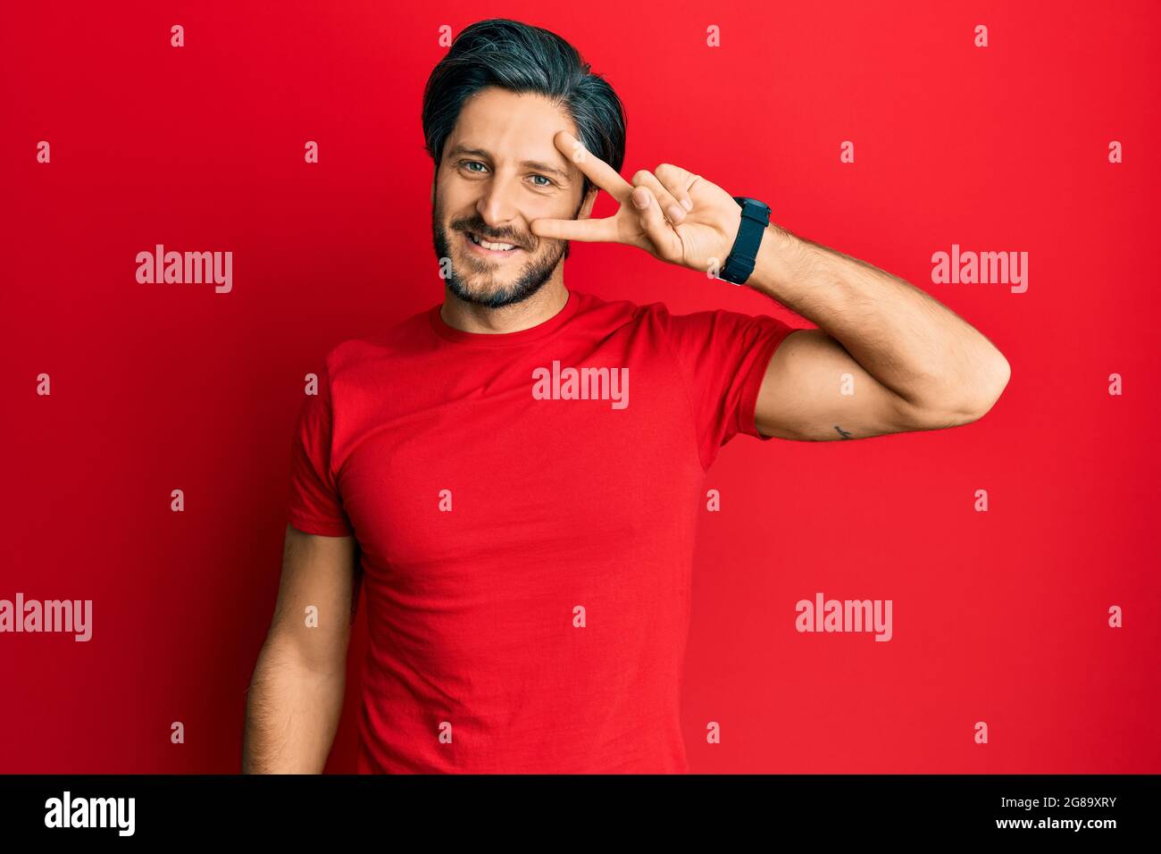 Young hispanic man wearing casual red t shirt doing peace symbol with ...