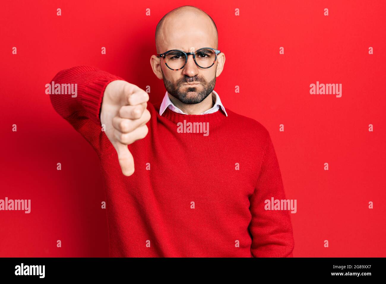 Young bald man wearing casual clothes and glasses looking unhappy and ...
