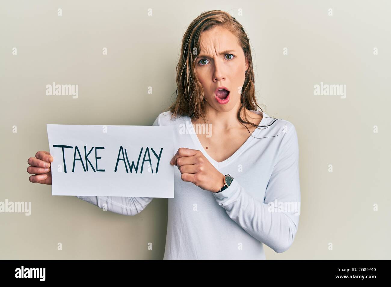 Young blonde woman holding take away food in shock face, looking ...