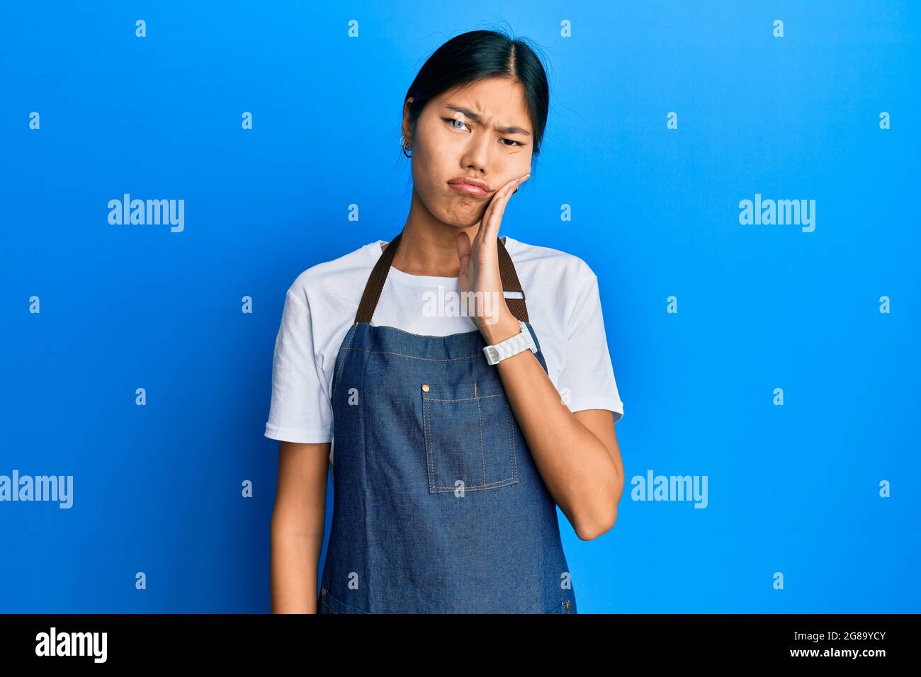 Young chinese woman wearing waiter apron touching mouth with hand with ...