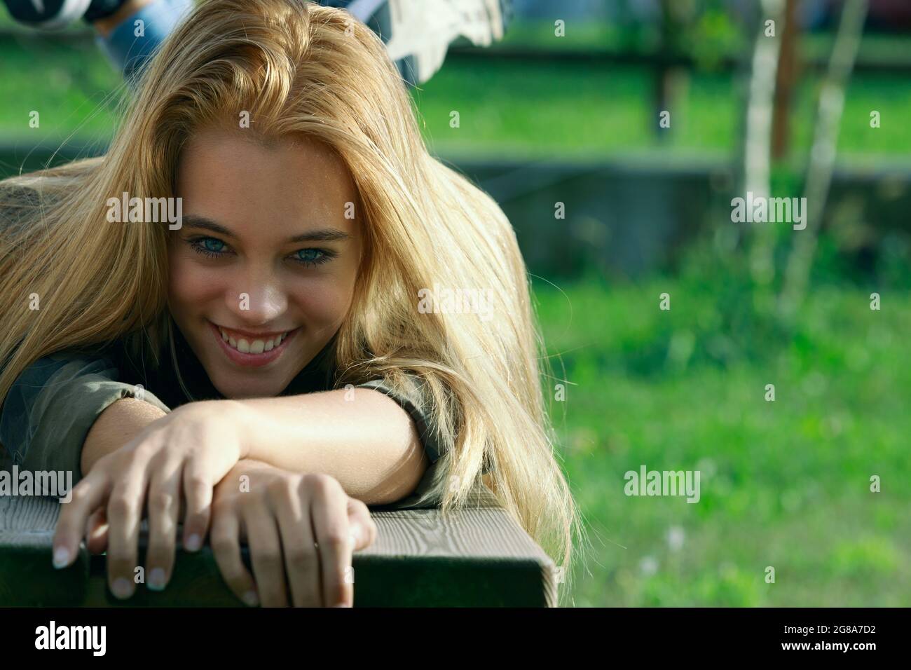 Cute young blond woman with a vivacious grin lying on her stomach on a ...
