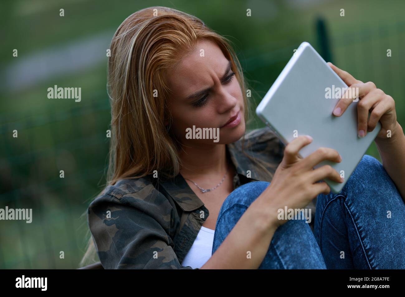 Concerned confused young woman staring at her tablet with a perplexed ...