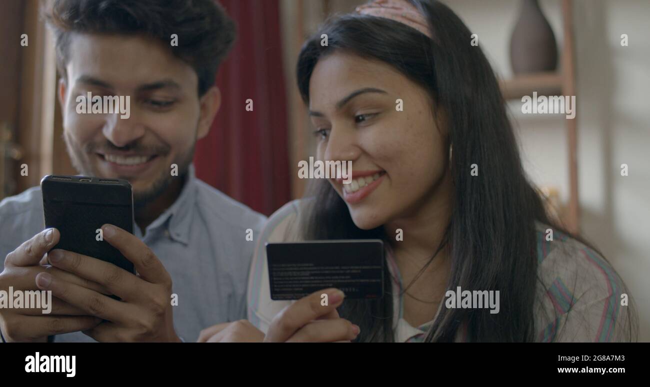 A young Indian woman helping her boyfriend to register bank card numbers on the phone Stock ...