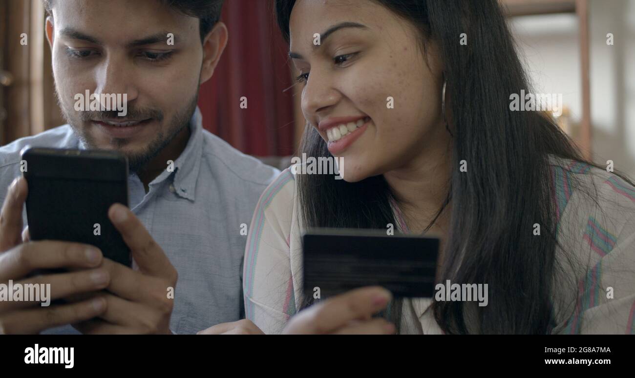 A young Indian woman helping her boyfriend to register bank card numbers on the phone Stock ...