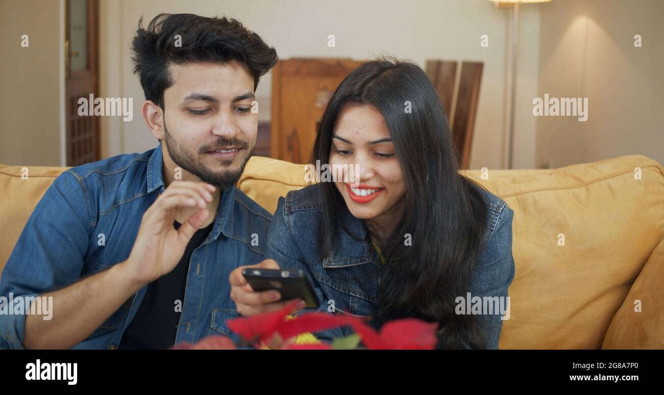 A young Indian couple happily doing a video call with a friend at home ...