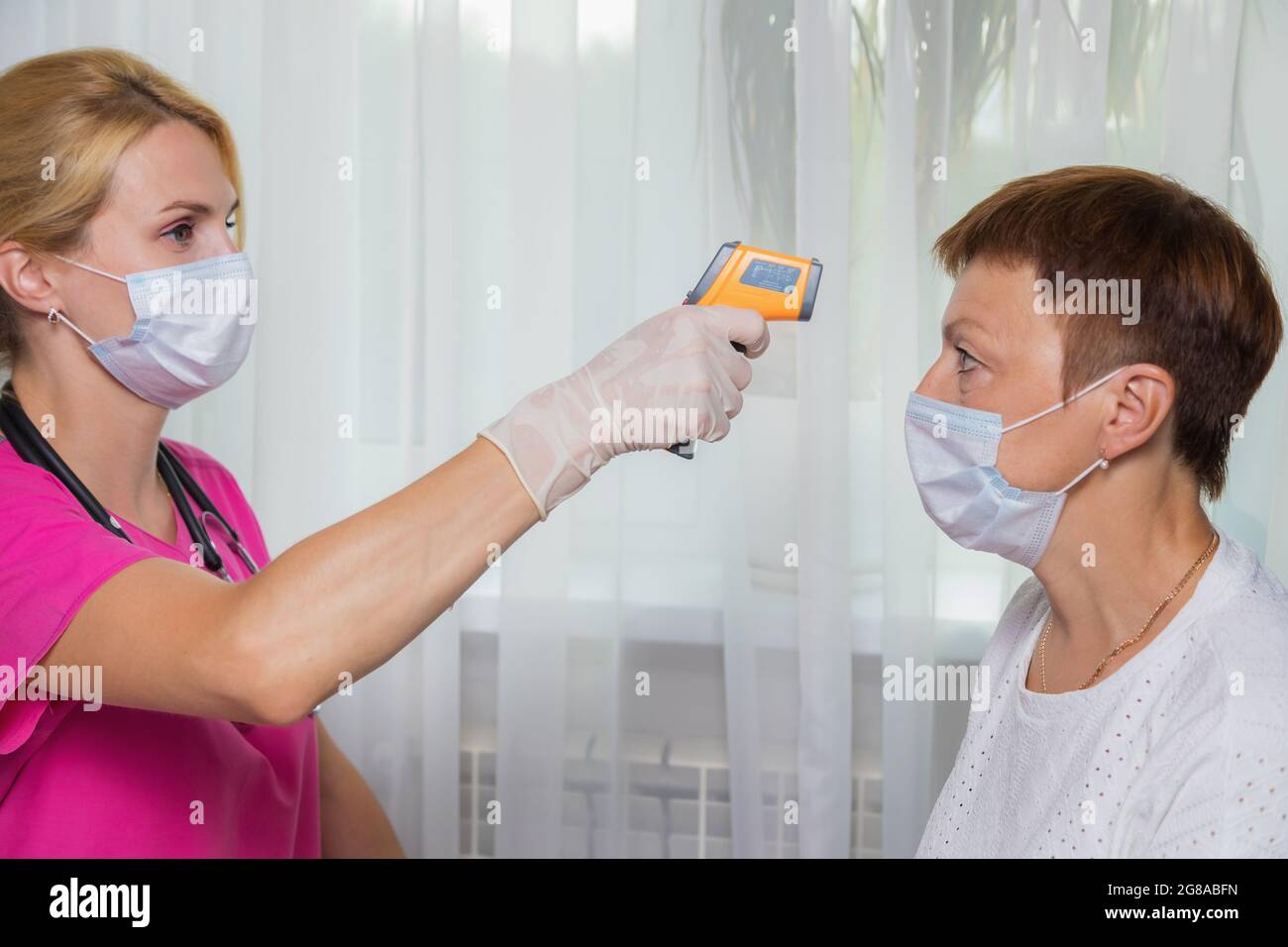 A female doctor measures the temperature of an adult woman with a laser ...