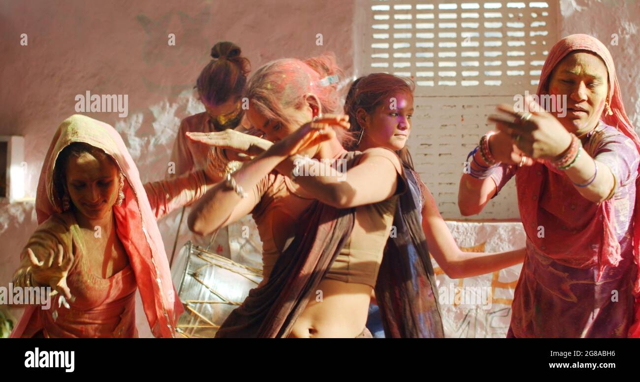 A group of females with painted faces and clothes are dancing at Holi ...