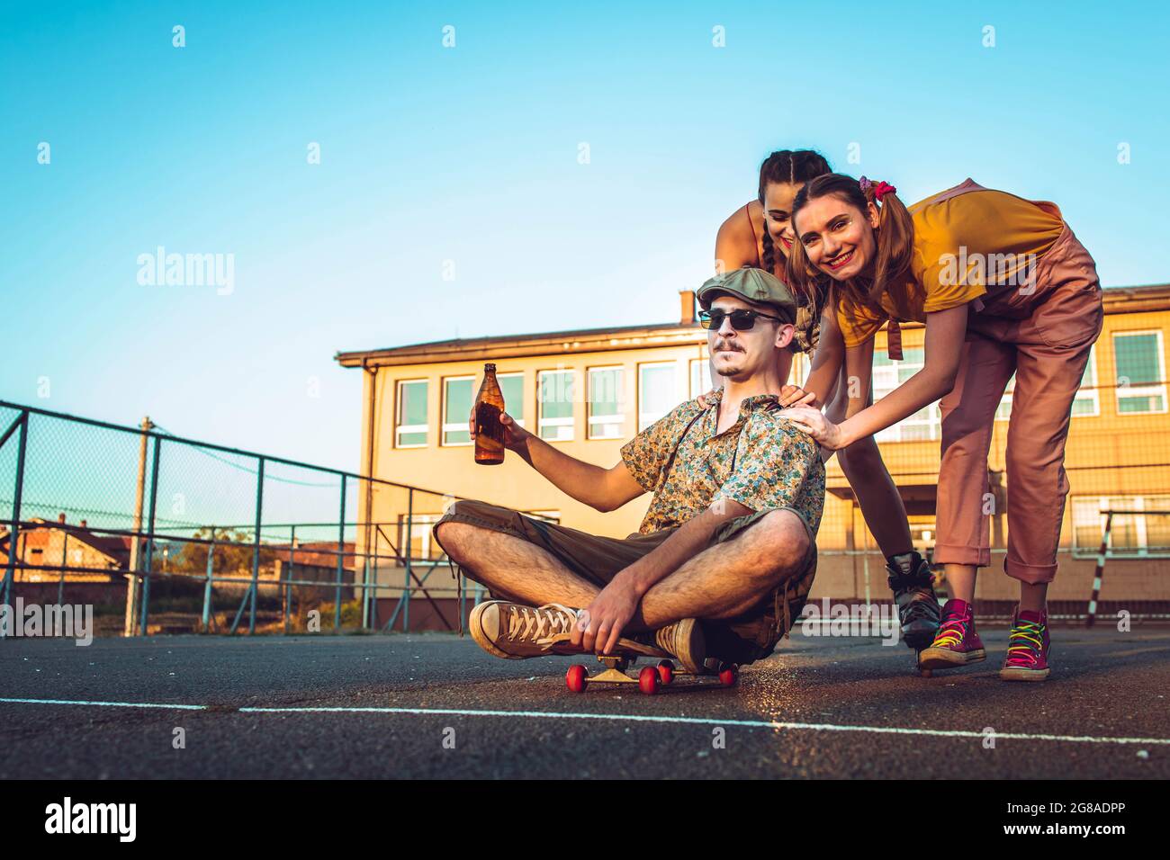 Group of friends hanging out outside. Two girls push their male friend ...