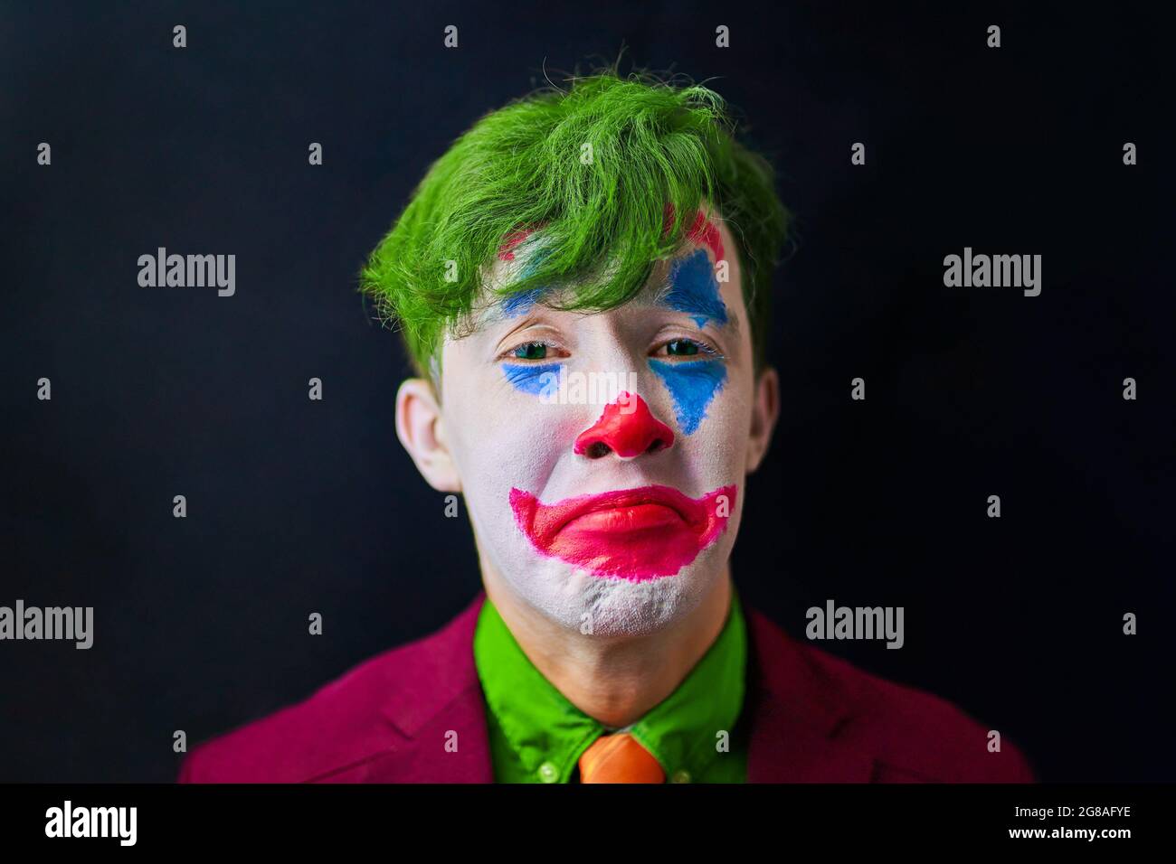 Man in mime makeup cosplay with green hair and a red suit an orange tie ...