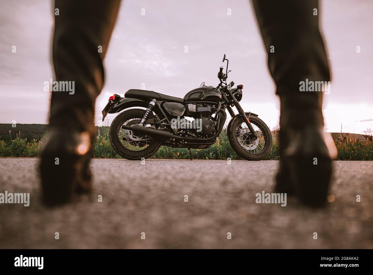 Legs of stylish motorcyclist woman standing near classic bike. Close-up ...