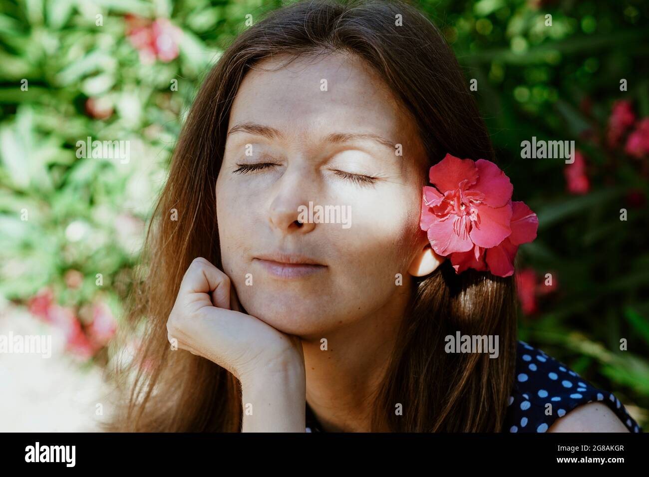 A beautiful Caucasian female with pink flower in hair with closed eyes ...