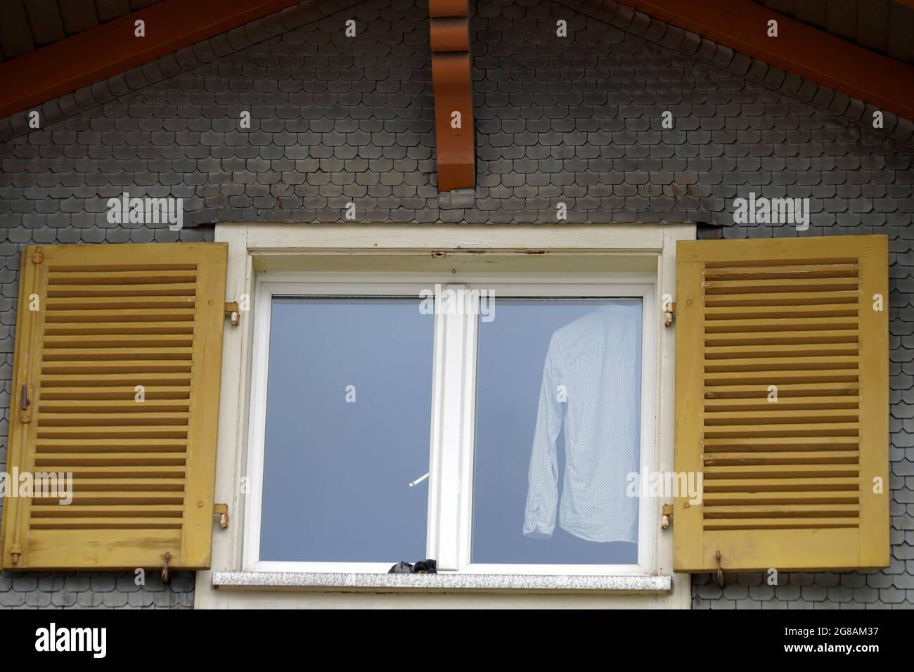 White shirt hanging in the window. The windows have yellow shutters ...