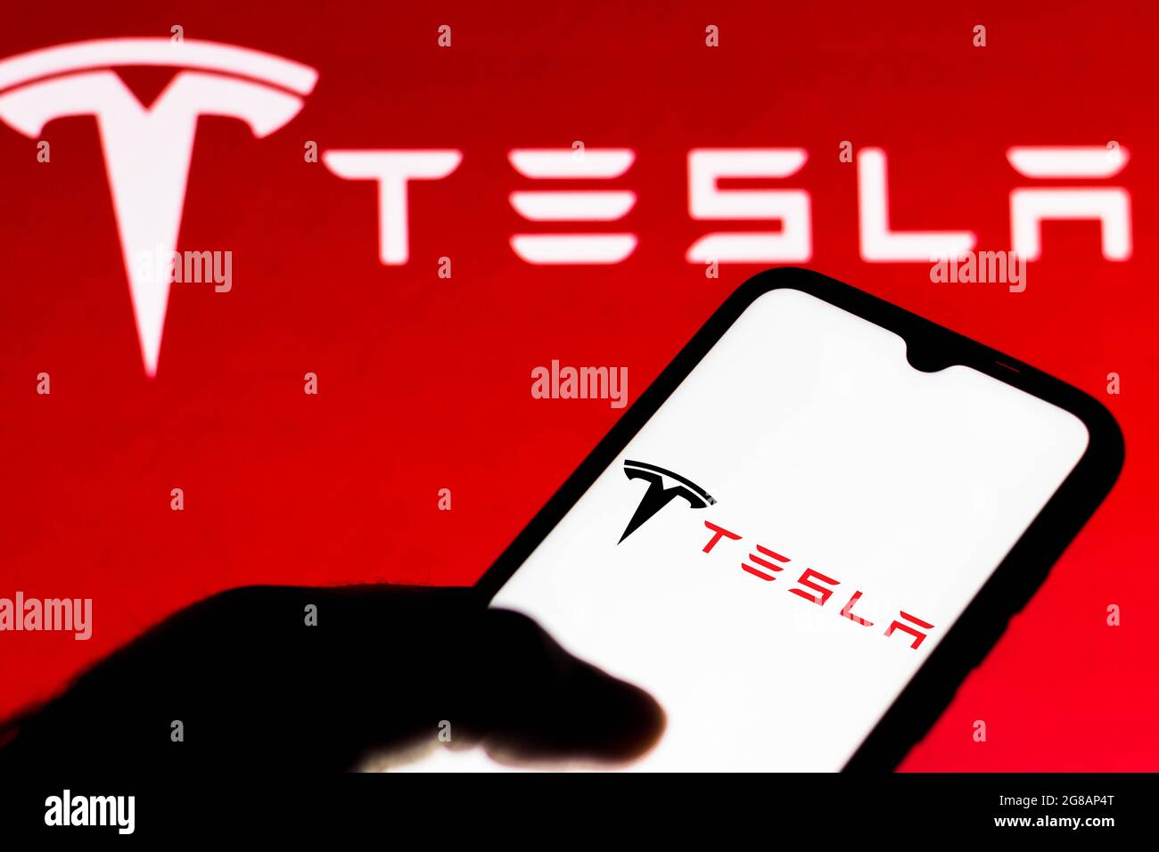 In this photo illustration the Tesla logo is seen on a smartphone and a ...