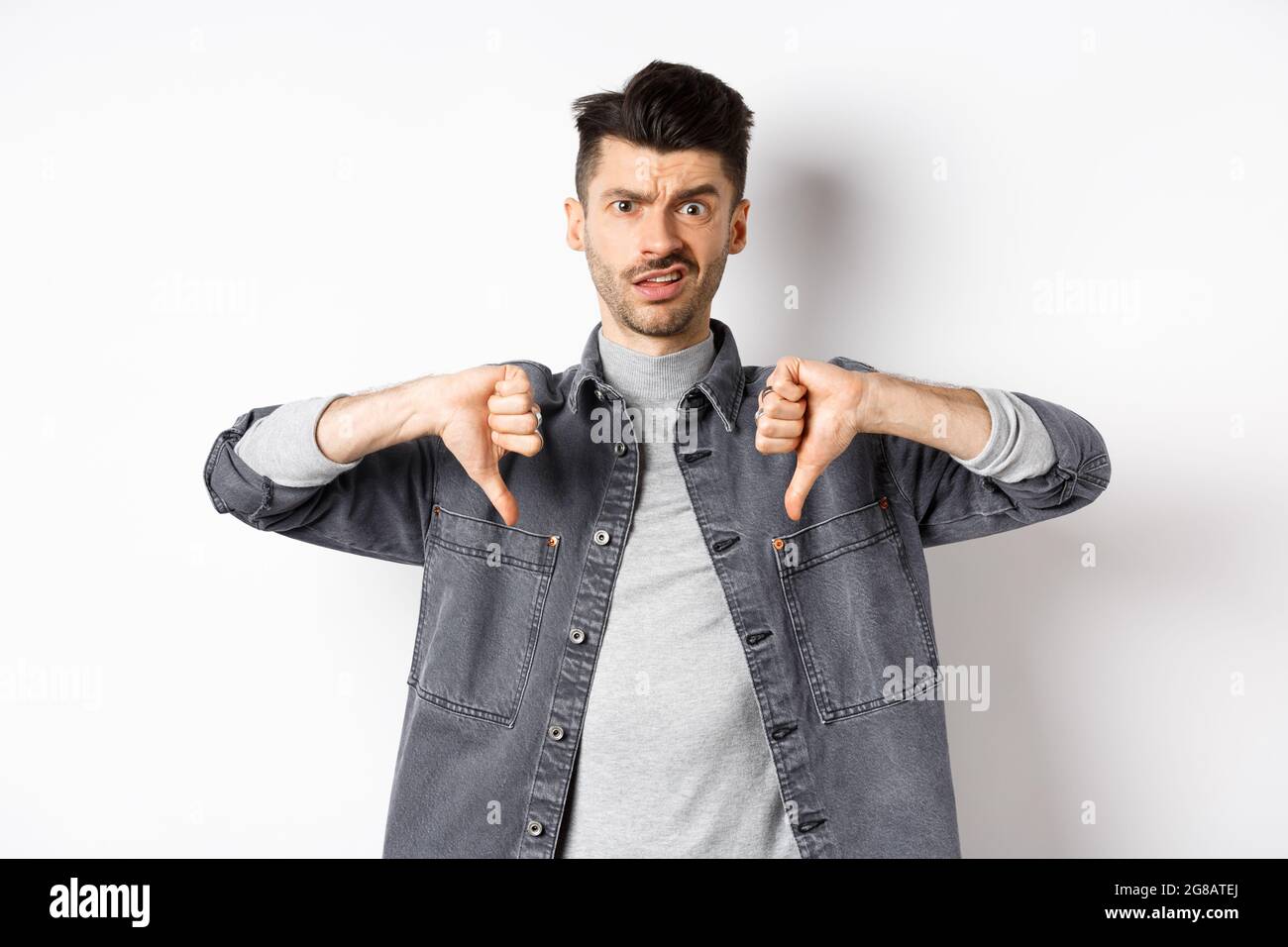 Disappointed guy showing thumbs down and frowning, looking skeptical at ...