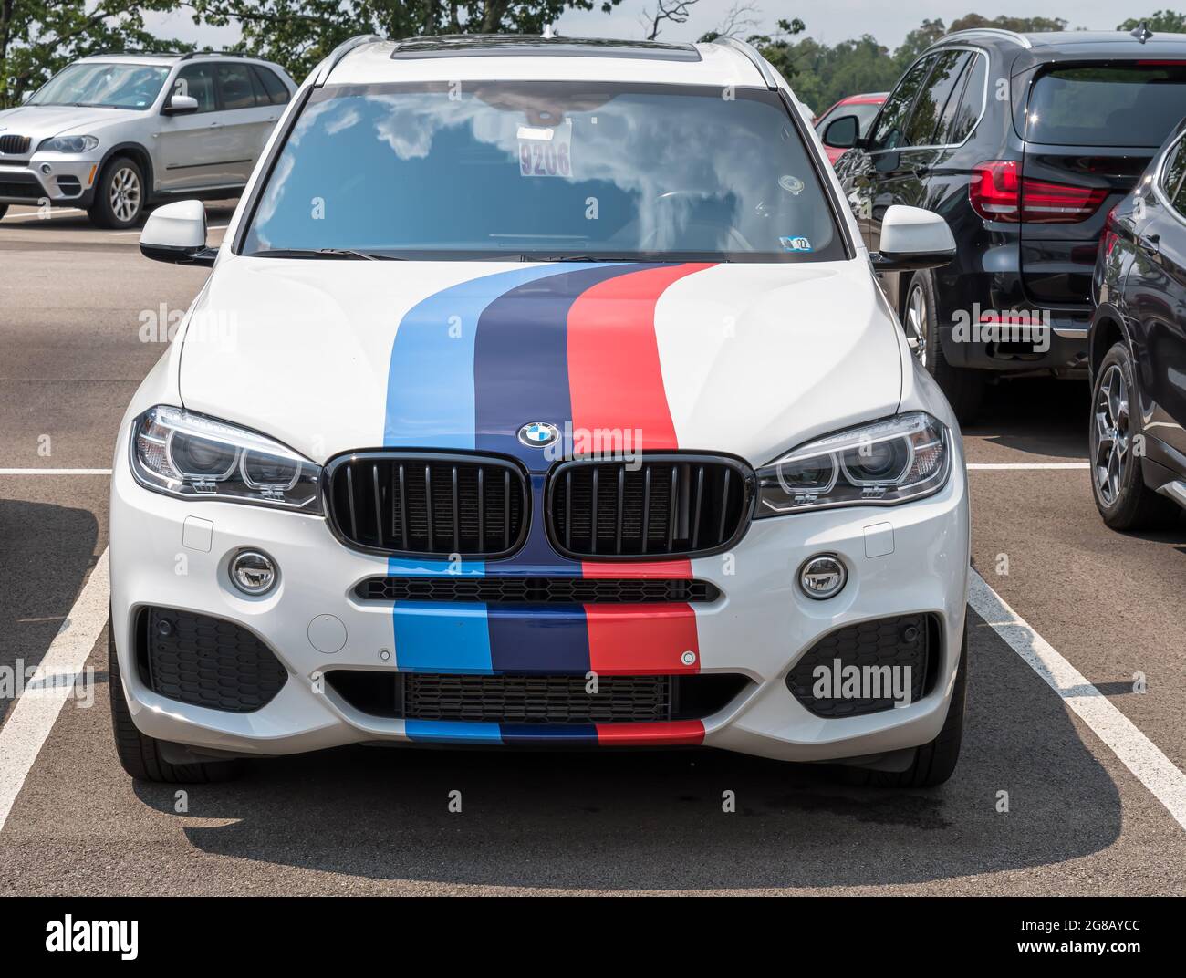 A white BMW SUV with multi colored stripes on the hood parked in a lot ...