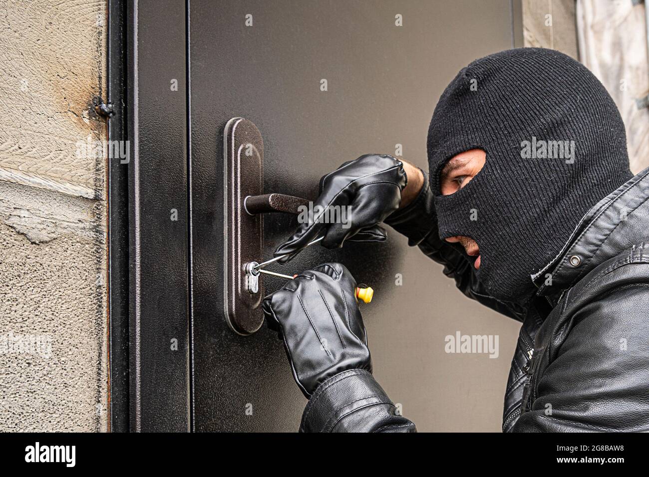 A man in a black balaclava mask opens a locked door with a lock pick ...