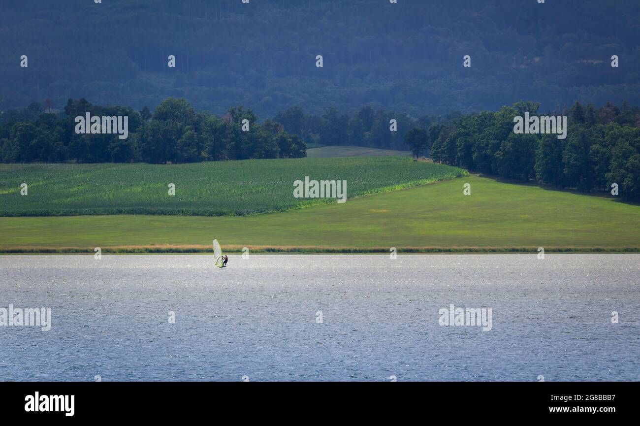 Windsurfer ride, sail on lake with distant hill and trees. Water sport ...