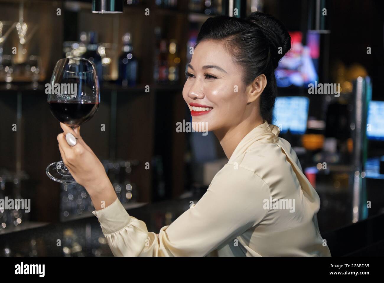Smiling elegant woman drinking red wine at bar counter in restaurant on ...