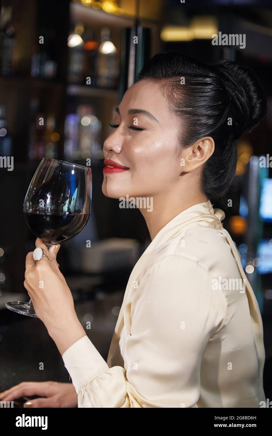 Pretty smiling woman enjoying wine tasting, she is smelling red wine in ...