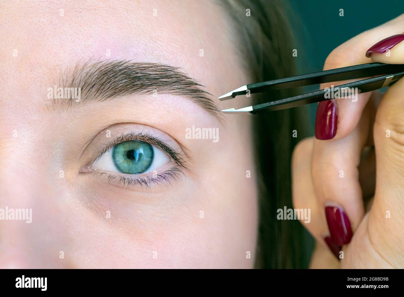 Beautiful young girl with eyelashes tweezing her eyebrows in a beauty ...