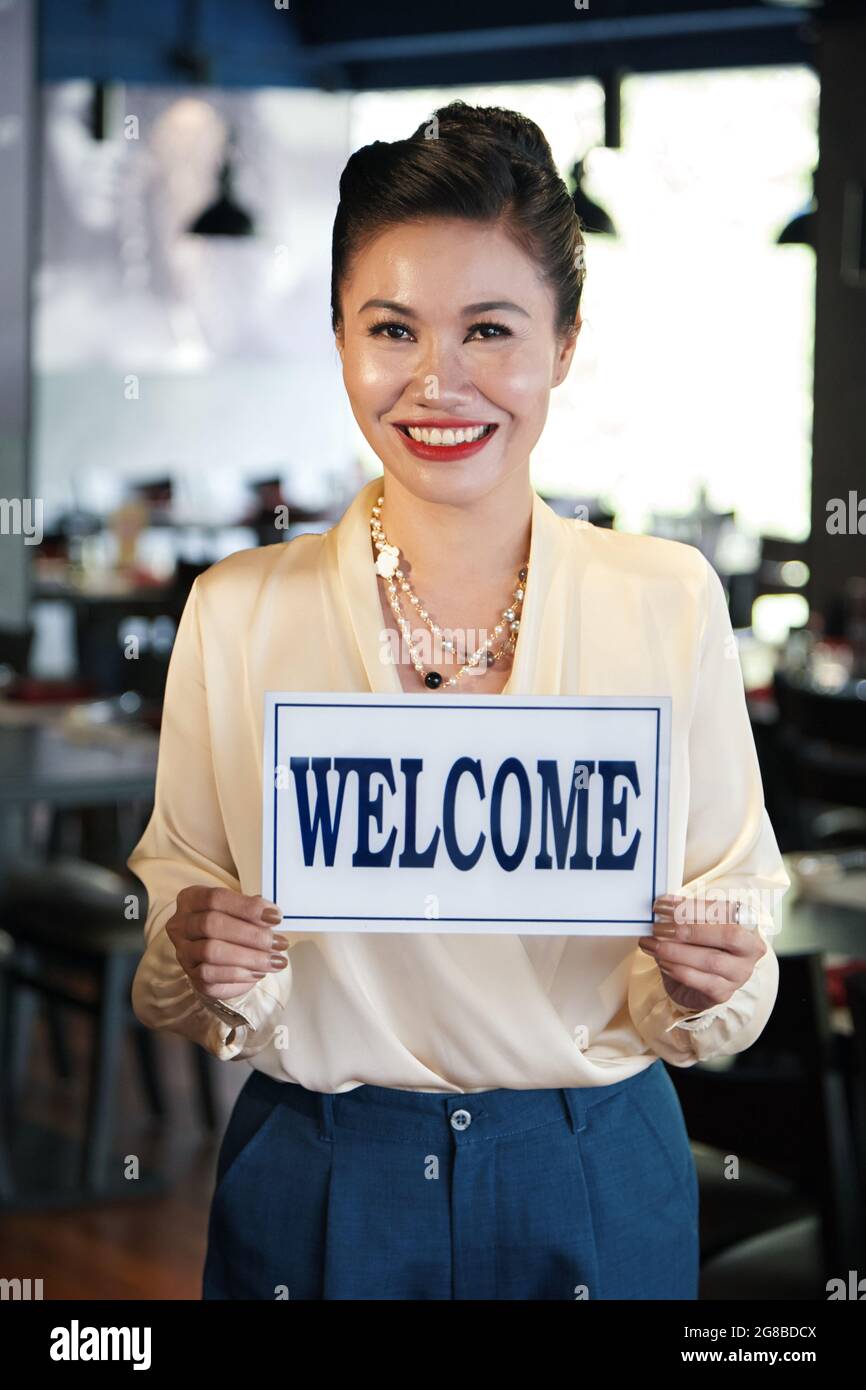 Portrait of happy smiling restaurant owner holding welcome sign in her ...