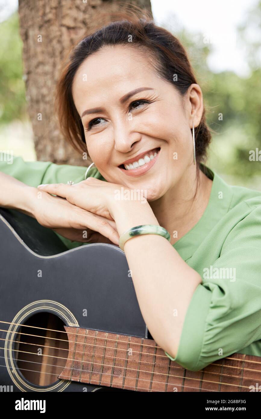 Portrait of smiling pretty senior woman leaning on acoustic guitar and ...