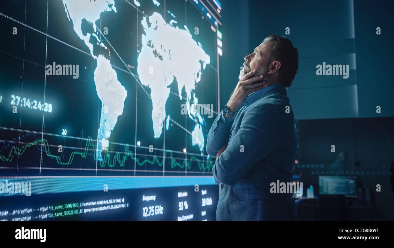 Senior Computer Science Engineer Looking at Big Screen Display Showing Global Map with Data ...