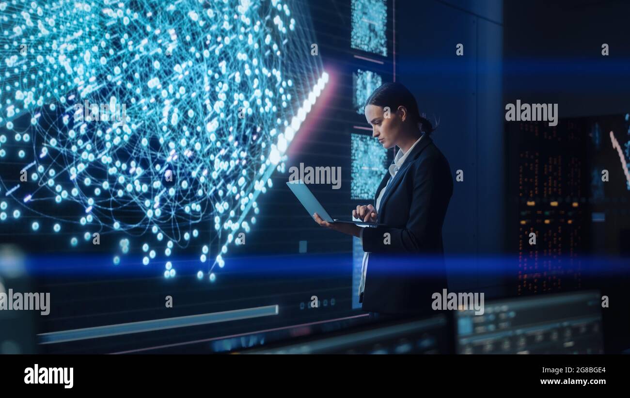 Young Female Computer Science Engineer Working on Laptop next at Big Screen Display Showing ...