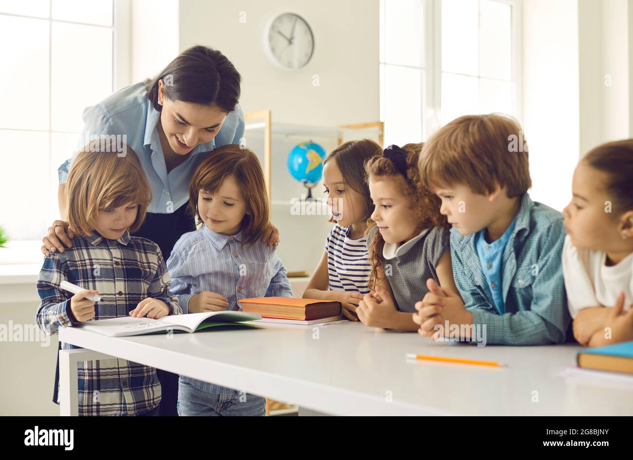 Young school teacher helping her happy little students who are learning ...