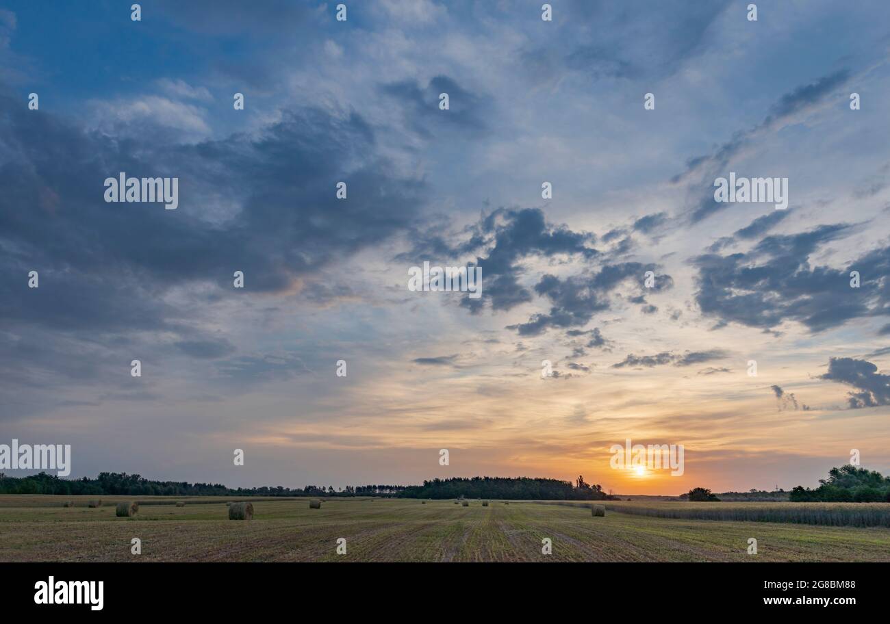 A rolls of hay in field at sunrise with amazingly beautiful clouds ...