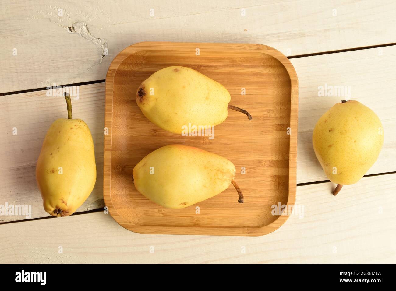 Four natural yellow pears with bamboo dishes, close-up, on a white ...