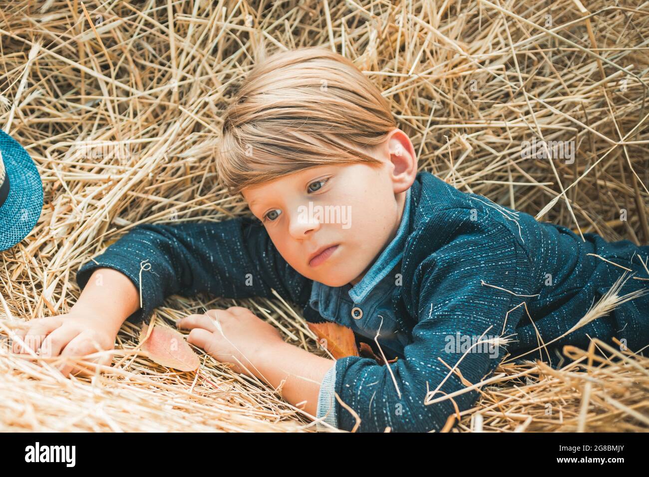 Kid boy lies on the hay. Cute little child boy holding gold leaf on ...