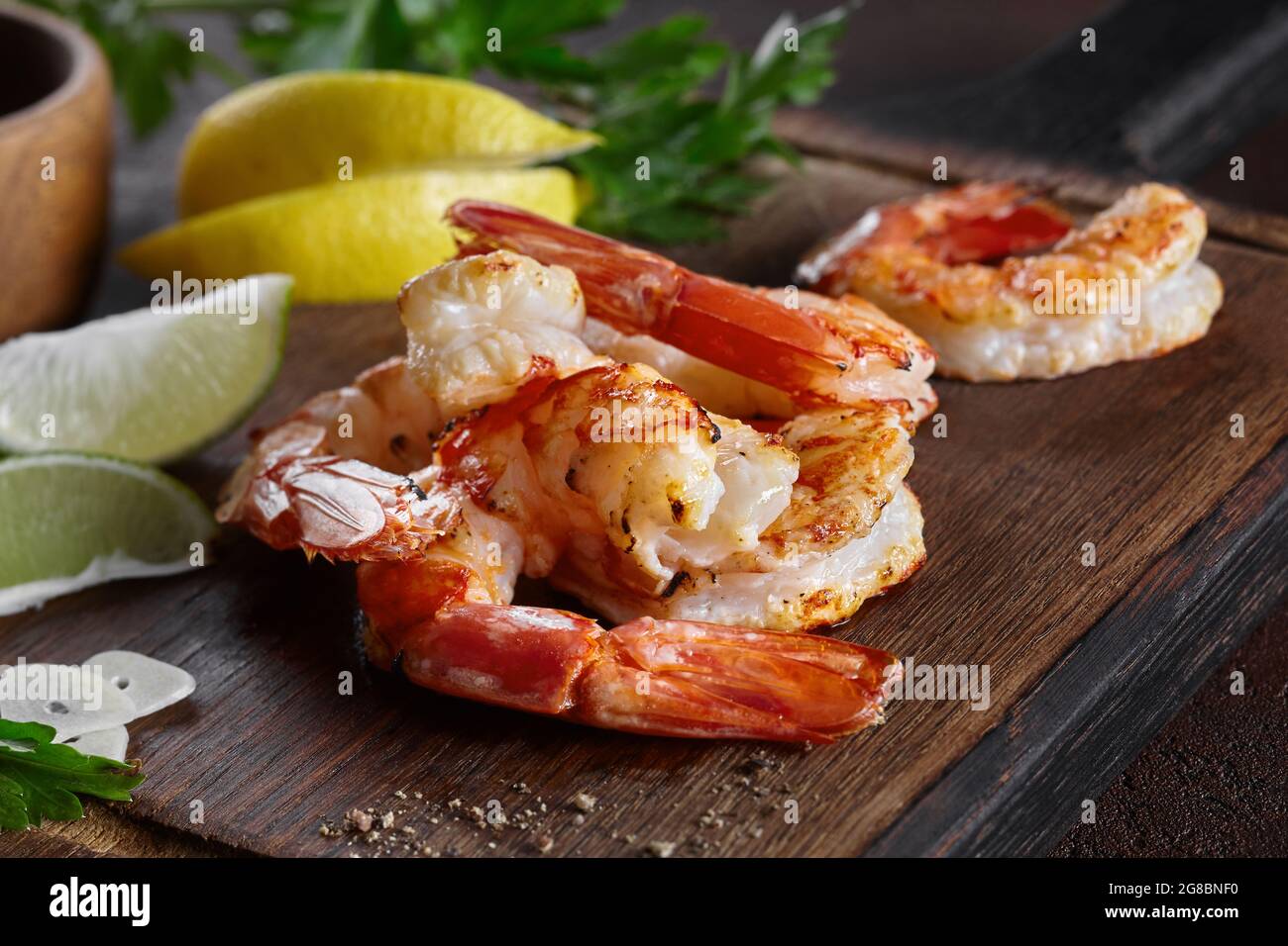 Grilled prawn tails with lemon, lime, garlic and greens on wooden board ...