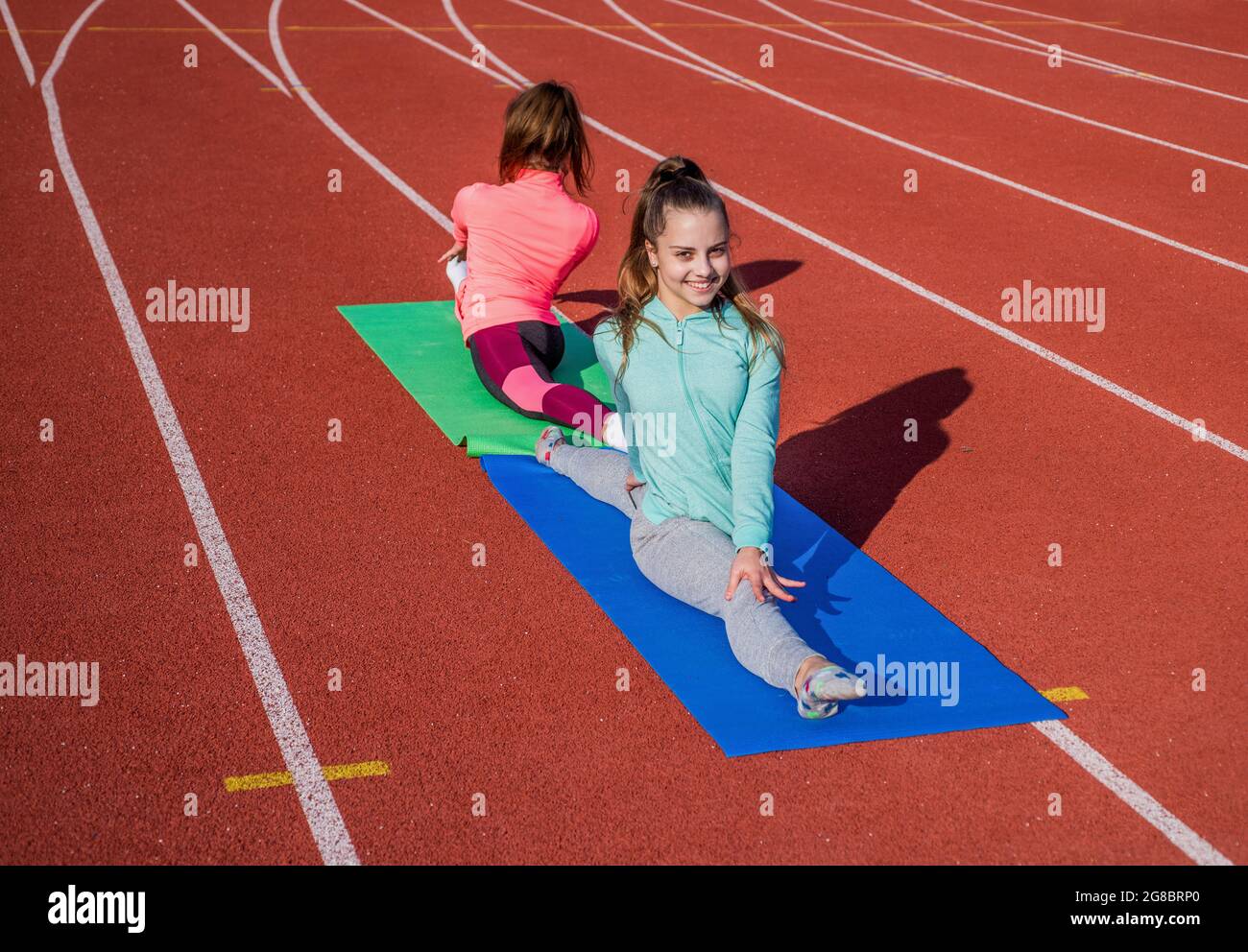 Happy fit girls do splits on stretch mat on athletics track, pilates ...